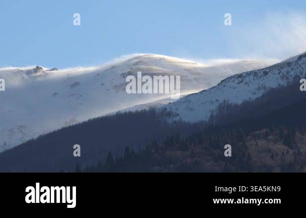 Strong blizzard wind sculpts snow surface across high mountain slope ...