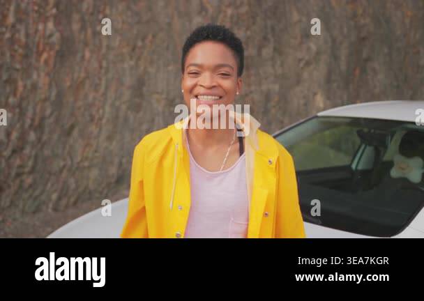 Smiling young person by car, wearing yellow jacket and casual tee short ...