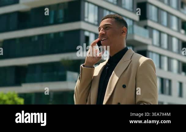 Cheerful African American business man speaking phone walking in city ...