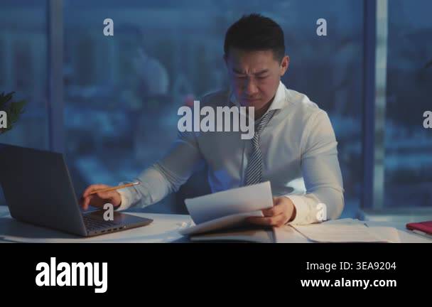 asian analyst late night financial review at cluttered desk, sorting ...