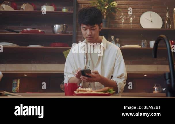 asian man checking phone while eating breakfast, scrolling messages on ...