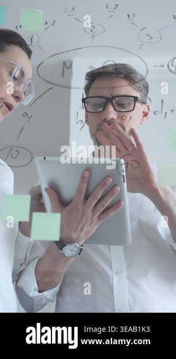 Business colleagues collaborating, writing and drawing on a glass board ...