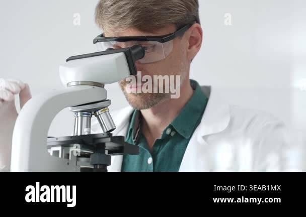 Adult male scientist wearing protective glasses and lab coat analyzing ...