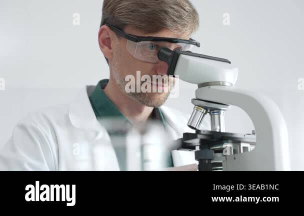 Adult male scientist wearing protective glasses and lab coat analyzing ...