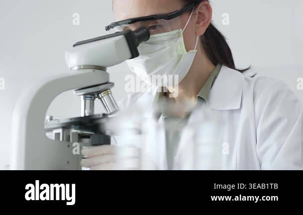 Female scientist wearing a lab coat, face mask and protective glasses ...