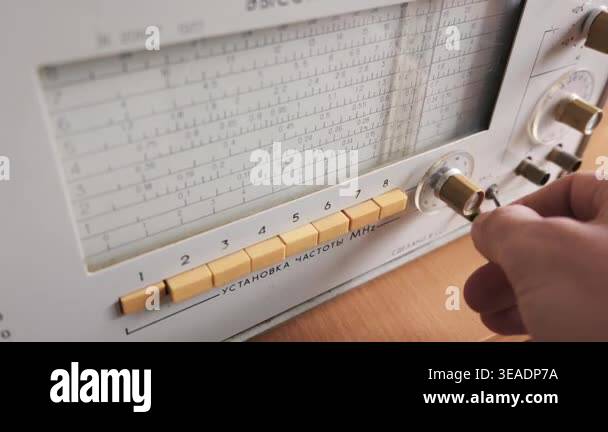 A hand carefully turns the tuning dial of an old analog Soviet ...