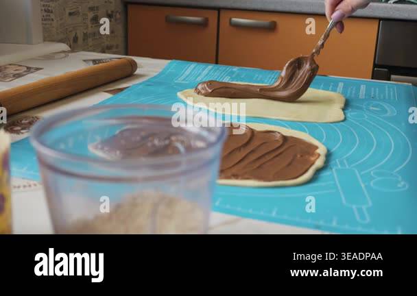 A close view of a hand spreading thick chocolate cream onto rolled ...