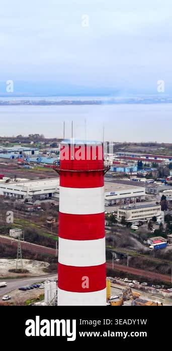 Red and white striped smokestack with light smoke against an industrial ...