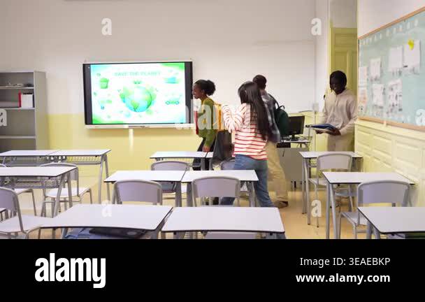 Diverse group of teenage students entering a classroom, greeting each ...