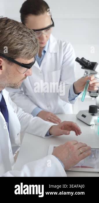 A male scientist takes notes on a tablet while his female colleague ...