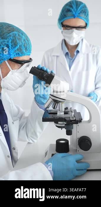 Two scientists in lab coats, face masks, and protective glasses ...