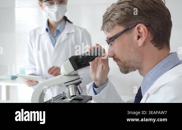 Scientific professional examining specimen through microscope ...