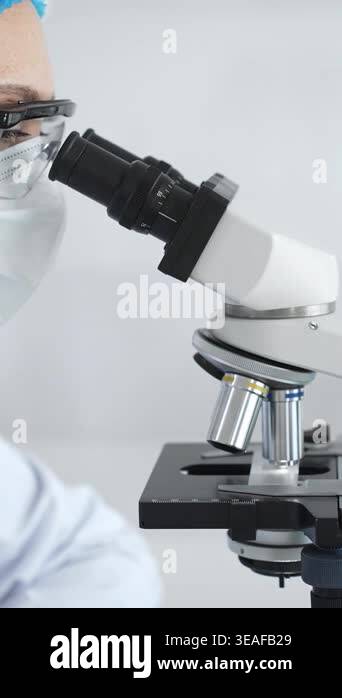 Female scientist wearing blue protective gear using a microscope ...