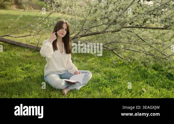 Beautiful young woman sitting barefoot on the lush green grass, reading ...
