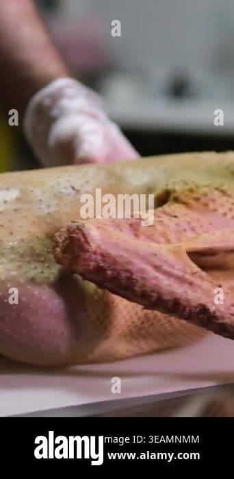 Male hands in white latex gloves cut raw duck on board over glass table ...
