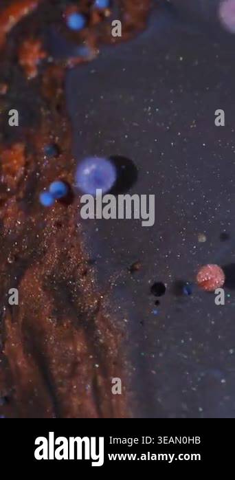 Vertical video. Ink spill. Glitter liquid. Defocused orange blue purple ...