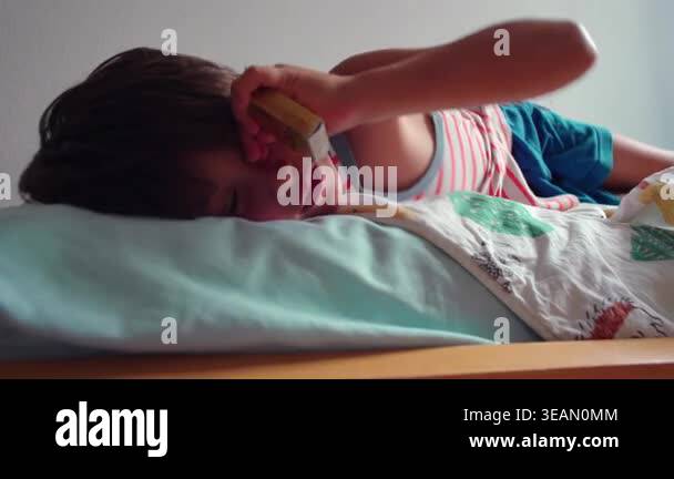 Young child resting on bed while rubbing tired eye and holding small ...