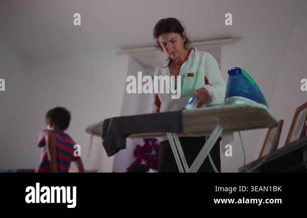 Parent pressing garment with steam iron while child handles clothing ...