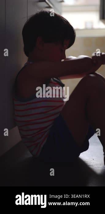 Young boy curled up indoors covering face with arms conveying sadness ...