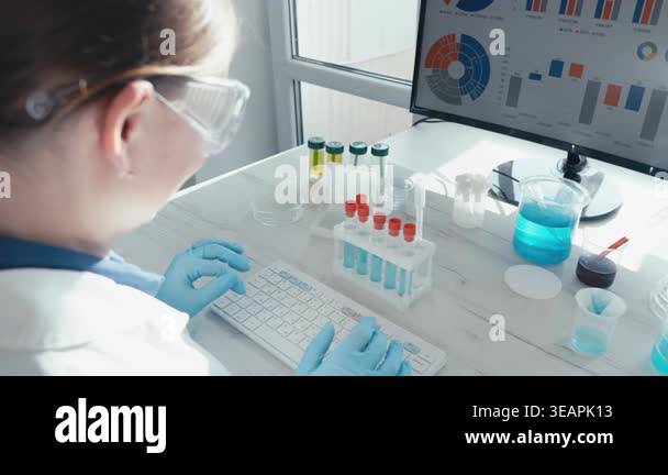 A researcher examines chemical samples in test tubes and enters data on ...