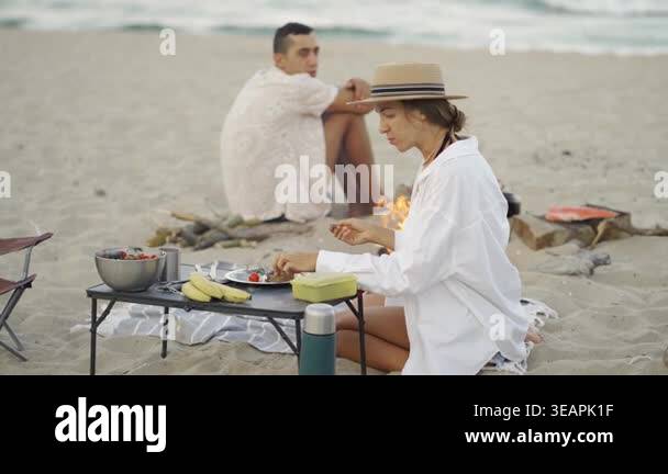Two people unwind on sandy shores, sharing a cozy beach picnic by a ...