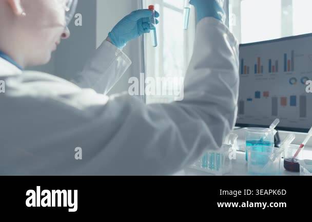 A laboratory professional examines chemical samples in test tubes ...