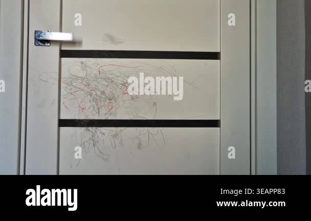 Child drawing with crayons on a white interior door, messy scribbles on ...