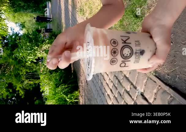 A hand holds a glass of bubble tea with a straw and stirs it. Street ...