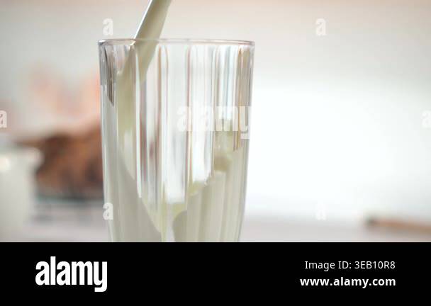 Fresh milk pouring into transparent glass with smooth splash, bright ...