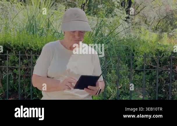 Elderly Caucasian woman reading an e-book on a park bench on a ...