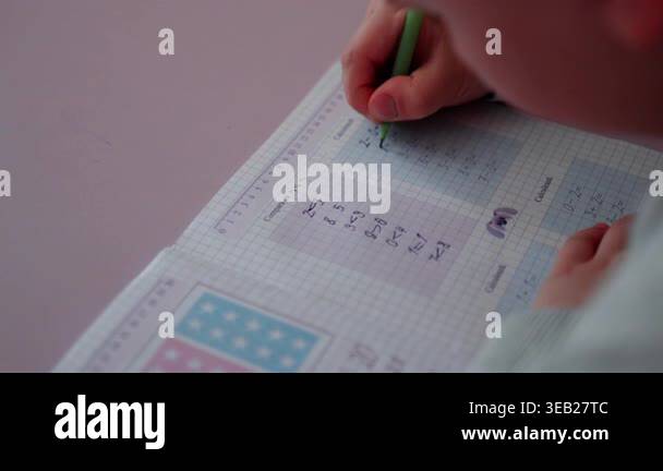 Child focuses on math exercises, writing with a green pencil on graph ...