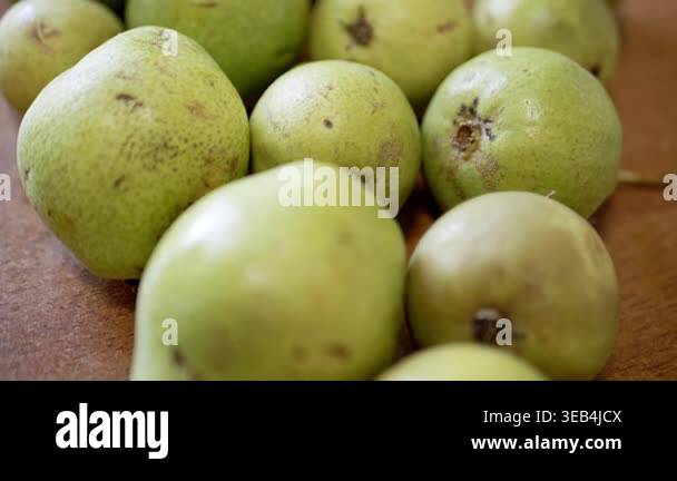 A group of ripe green pears rests on a brown wooden surface in a close ...