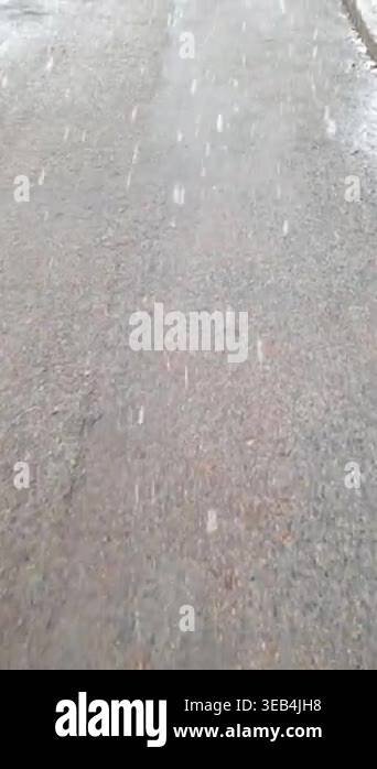 Snowflakes fall on a dark, wet asphalt road during a light flurry. POV ...