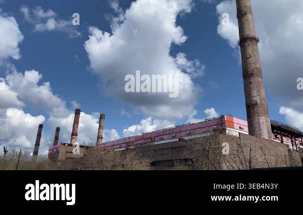 Old industrial factory with tall chimneys against blue sky with clouds ...
