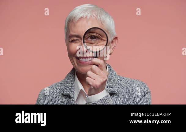 Portrait of a smiling senior woman holding a magnifying glass over one ...