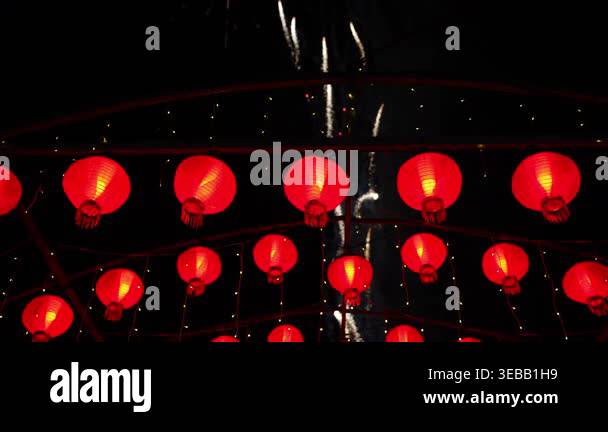 Ground-level view of glowing red lanterns hung under fireworks at a ...