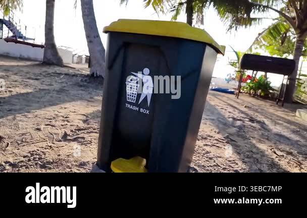 This video features a black trash can on a sandy beach with palm trees ...