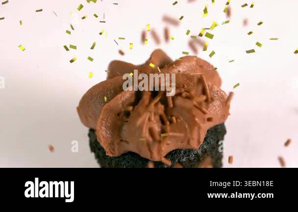 Offscreen dispenser releasing brown jimmies and gold confetti, cupcake ...
