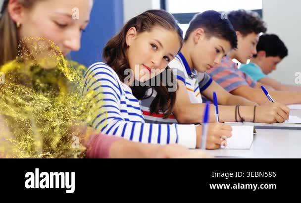Center student holding pen, glancing and smiling at gold particles ...