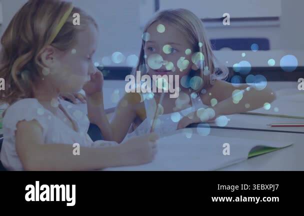 Girls sitting at school desk, right girl leaning, pointing, sharing ...