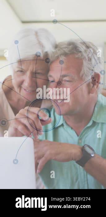 Senior pair sitting, man holding blue disc leaning, pointing at laptop ...