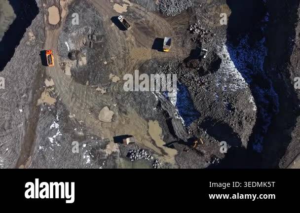 Workers and heavy machines are busy at a granite quarry. Trucks ...