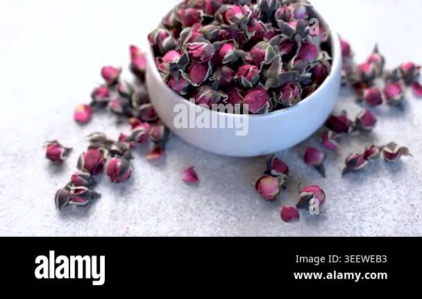 Dried tea rosebuds in a white ceramic bowl rotating on a white concrete ...