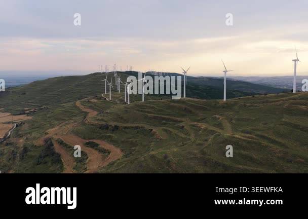 Wind turbines turning on a green hillside during a beautiful sunset ...