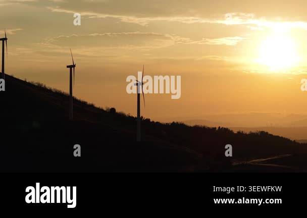 Silhouetted wind turbines spinning on a mountain ridge with a golden ...