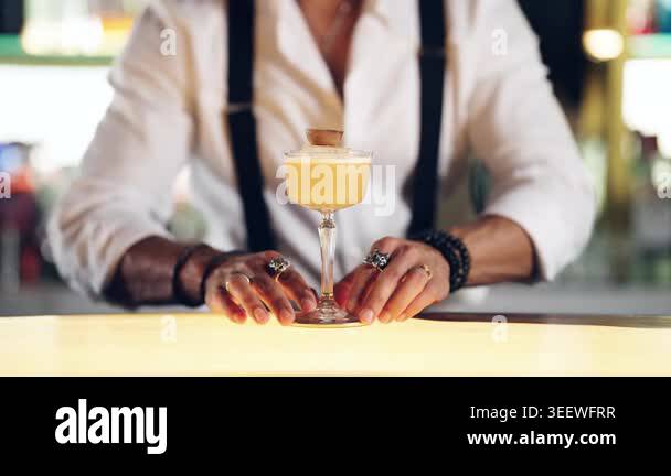 Stylish bartender with rings and suspenders serving a frothy yellow ...
