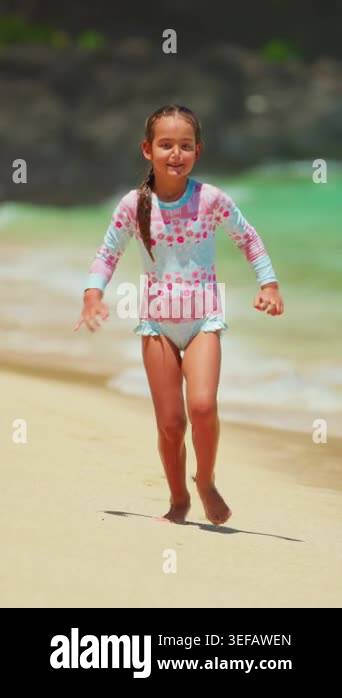 A cute little girl is happily running along the ocean shore with ...