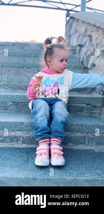 Cute little girl eating ice cream while sitting on stone steps in the ...