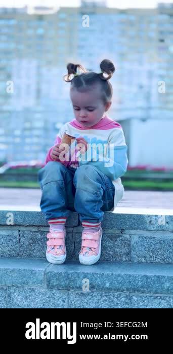 Cute little girl enjoying an ice cream cone while sitting on outdoor ...