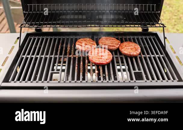 Close up view of four burger patties cooking on open barbecue gas grill ...